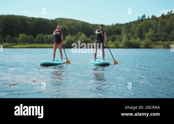 Smiling man and woman standing on sup board and swims surfing on the ...