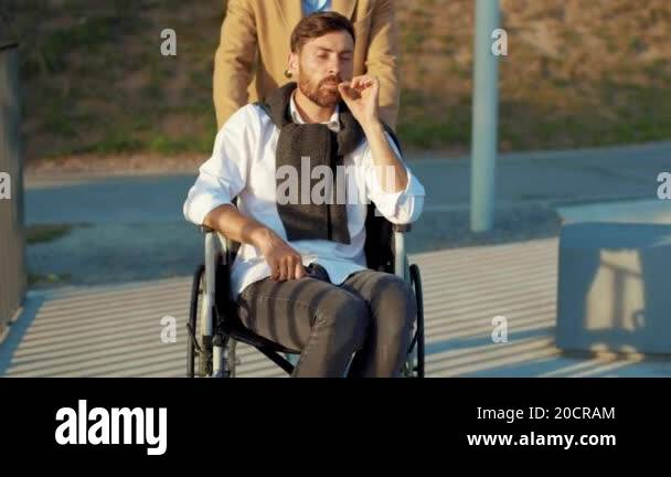 At sunlight man have fun on a wheelchair ride smoking weed and smiling ...