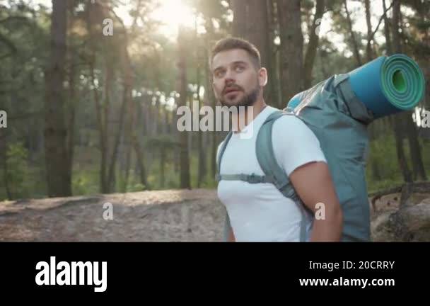 Close up of the handsome young man hiker standing in the forest turning ...