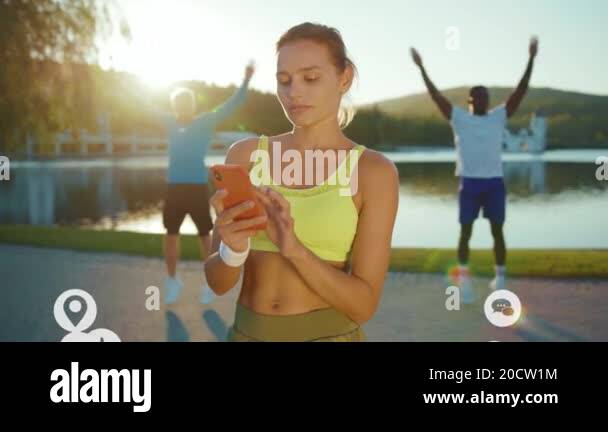 Portrait smiling woman stand use phone in sportwear outdoors. Fitness ...