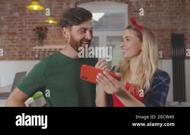 Funny young couple use smartphone talking stand at kitchen on home ...