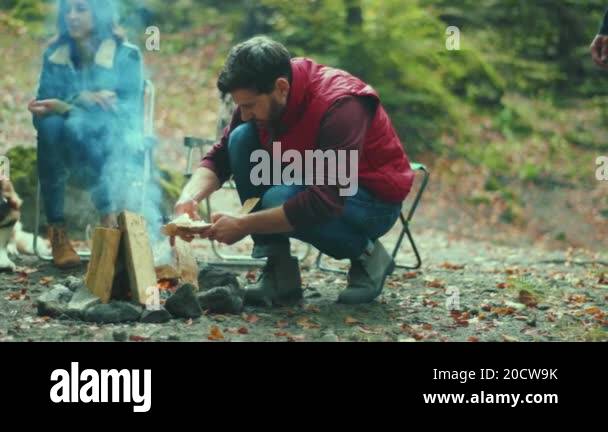 Close up father with family in the woods sets up campfire sticks ...