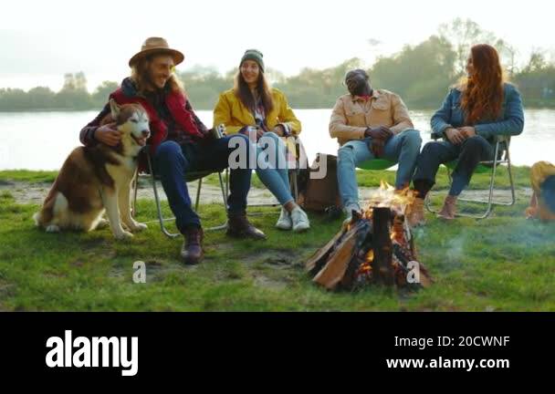Slow motion friends sitting near campfire in nature. Young people talk ...