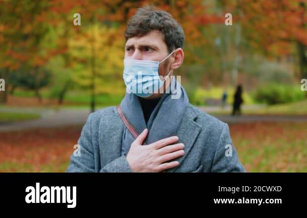 Portrait sick young man with sad face and a protective mask coughs ...