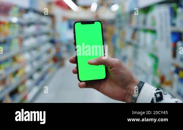 Close up man hand use mobile smartphone with vertical green screen in supermarket blurred ...