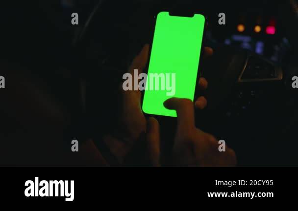 Close up young hands man use holding smartphone with vertical green screen in car at night ...