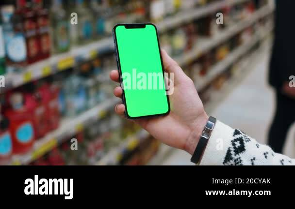 In supermarket hands man use hold phone with vertical green screen blurred background. Indoors ...