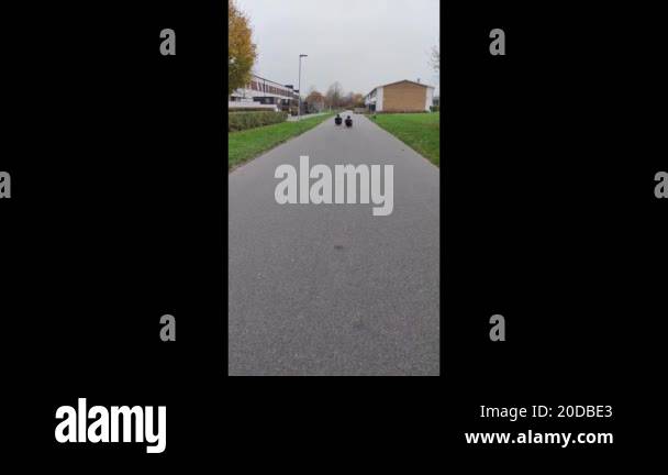 Two children ride along a road in small carts, while a third rides a ...