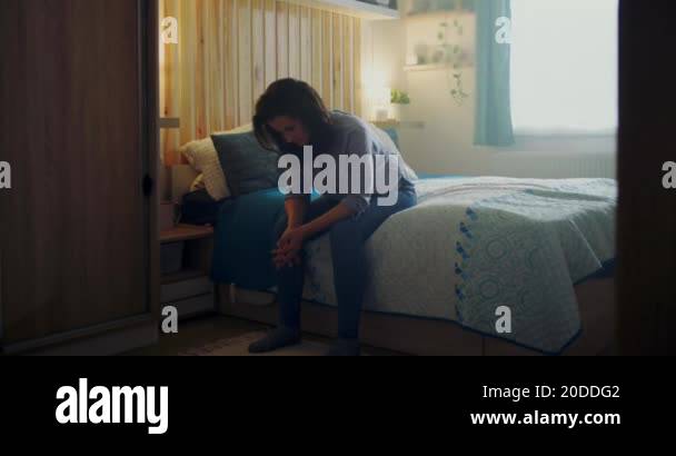 Woman sitting on a bed, leaning forward with her face buried in her ...