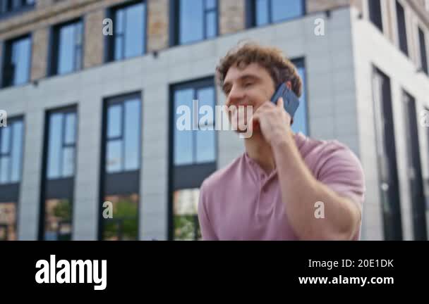 Positive student talking smartphone walking near modern city building ...