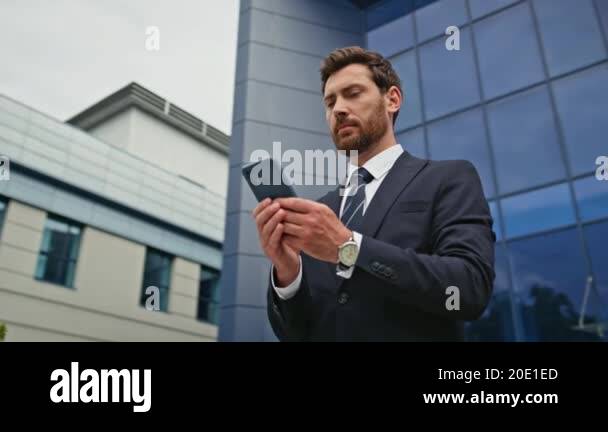 Serious director checking smartphone in front city office building ...