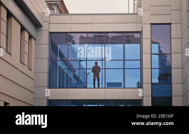 Contemplative businessman standing at window modern office overlooking ...