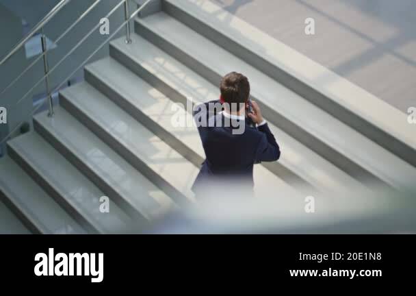 Businessman climbing staircase talking smartphone at luxury corporate ...