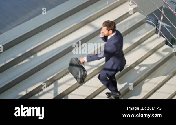 Motivated businessman calling smartphone climbing stairs bright office ...