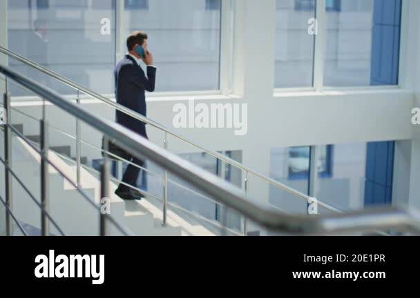 Bearded employee talking cellphone descending bright office stairs ...