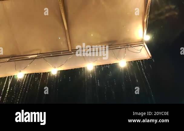 Raindrops dripping from yellow roof with shining lanterns against black ...