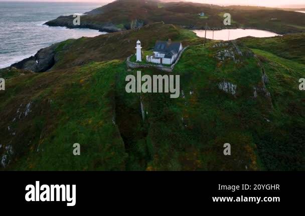 A lighthouse on a green cliff overlooks the serene sea, embodying the ...