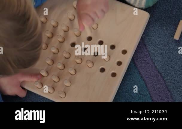 Young child plays with wooden solitaire game, top view. Toddler ...