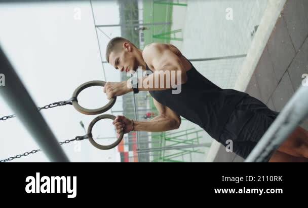 Handsome sporty guy doing exercising with gymnastic rings. Man building ...