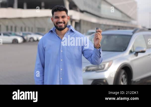 Attractive male driver pointing at keys from new car. Portrait of ...