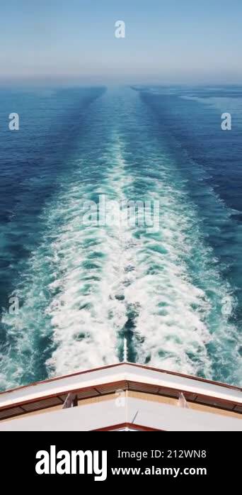 A ship sails in the ocean and leaves a white trail in the blue waters ...