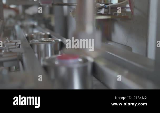 An automated mechanism in the production line fills tin cans with paint ...