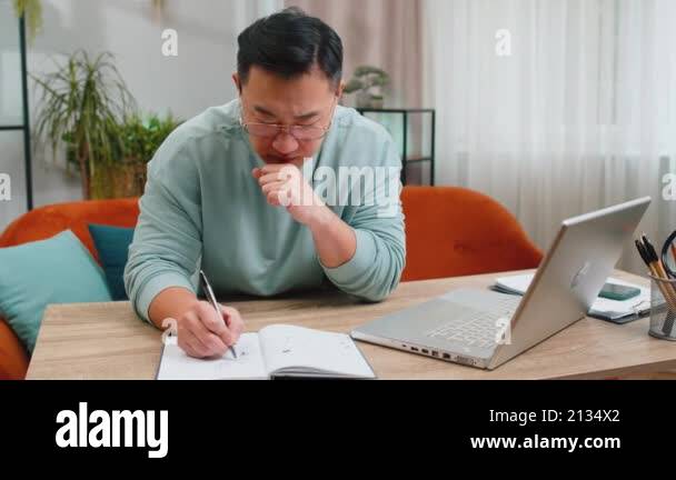 Asian man freelancer making notes on notebook at home, use laptop ...