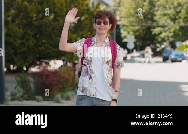 Cheerful young man tourist smiling friendly at camera, waving hands ...