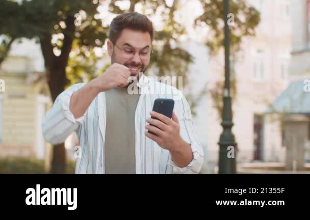 Excited amazed Caucasian man outside using mobile phone device winning online shocked male ...