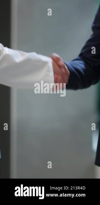 Vertical Screen: Close-up of a handshake between a doctor in a white ...