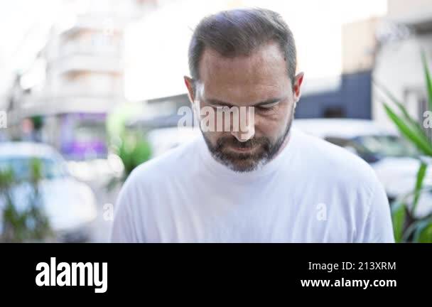 Handsome middle-aged hispanic man smiling outdoors on a city street ...
