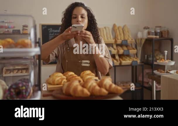 Young woman with curly hair takes a photo of croissants in a bakery ...