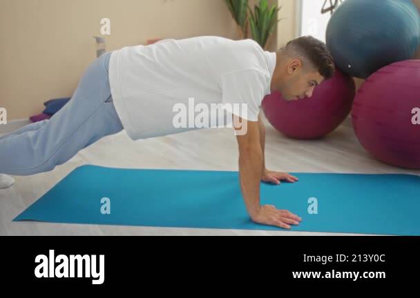 Young man exercising on a blue mat in a gym center performing mountain ...