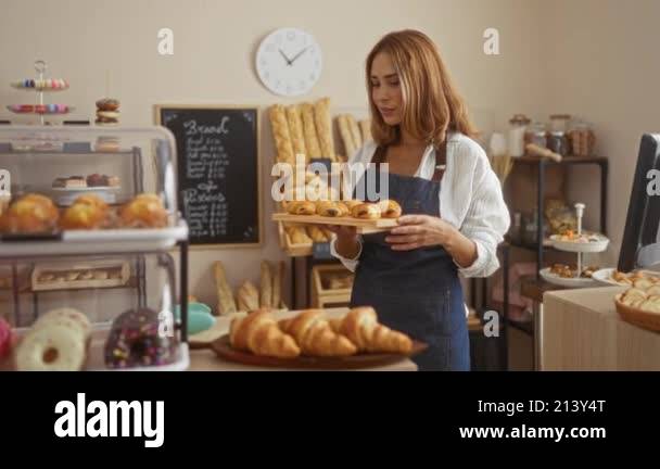 Brunette woman in bakery holding pastries while wearing an apron with ...