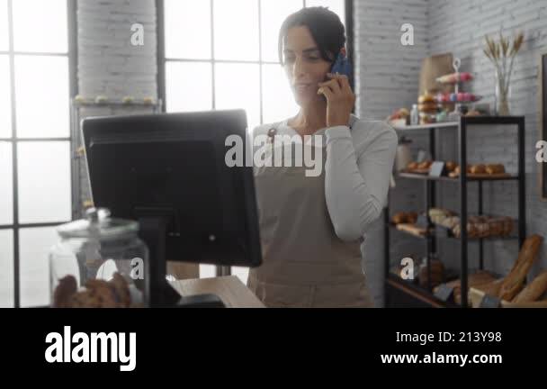 Woman working at a bakery while talking on the phone, standing behind a ...
