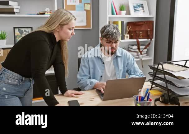 Man and woman collaborate using laptop in modern workplace setting, exemplifying teamwork and ...