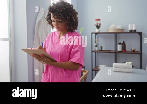Woman working at a spa in a pink uniform, taking notes on a clipboard ...
