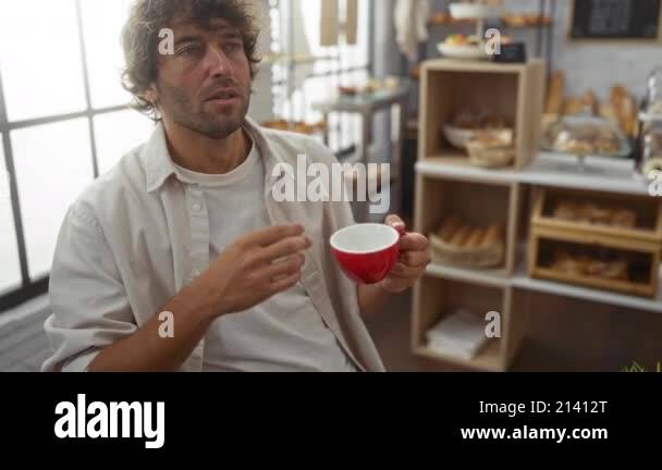 Young man in shocked expression, drinking coffee at a coffee shop table ...