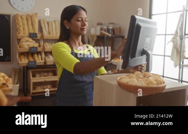 Woman working in a bakery using a computer with fresh bread on display ...