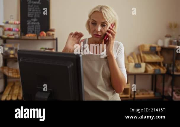 Woman talking on phone in bakery shop with bread shelves in background ...