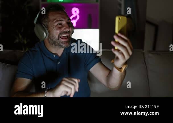 A middle-aged man video calling with headphones at home, exuding a ...