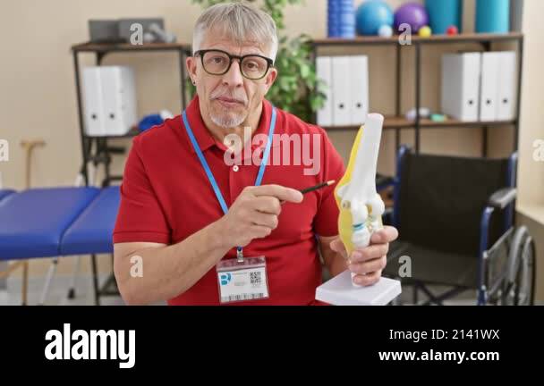 Mature man in glasses explaining human bone anatomy in clinic interior ...