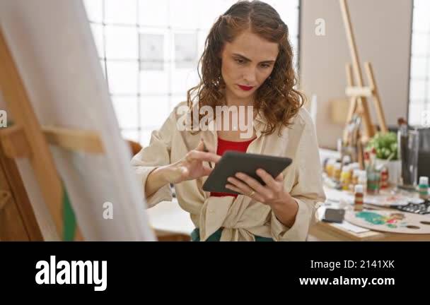 Young, relaxed woman artist seriously draws on touchpad, looking at her ...