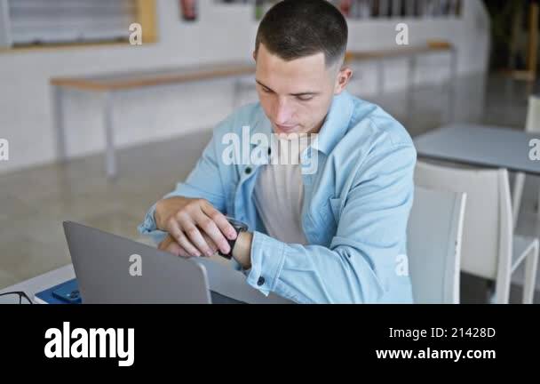 Hispanic man checking time on wristwatch while working with laptop at ...