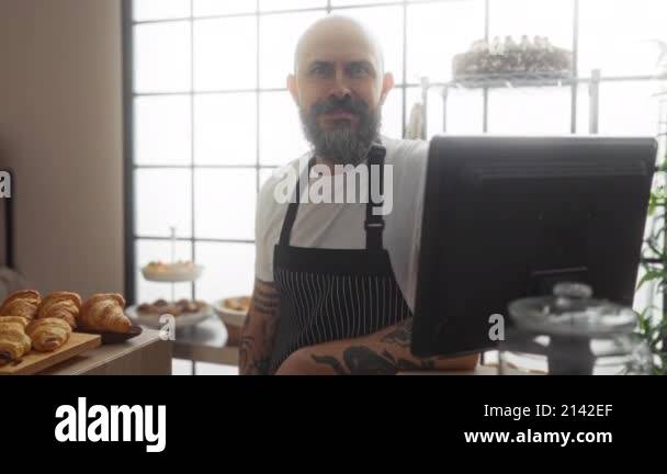 Bearded man working at bakery with pastries in background and bright ...