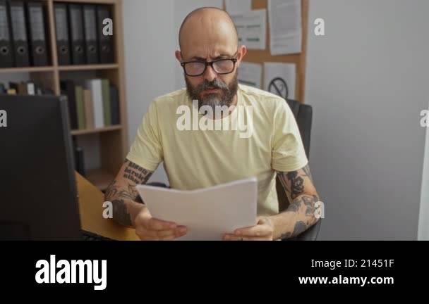 Man with beard and tattoos analyzing documents in office setting, bald ...