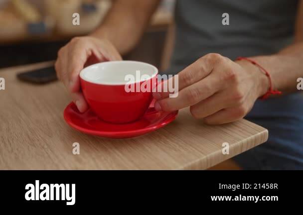 Young man enjoying coffee in a cafe, holding a red cup with a wooden ...