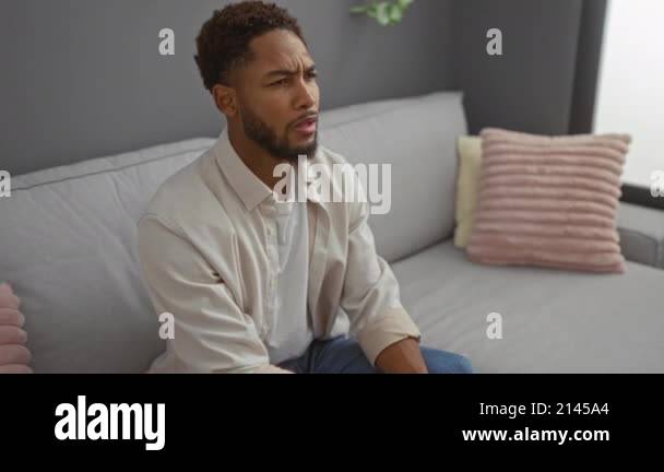 Young man expressing shock and disbelief while sitting on a couch in a ...