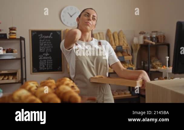 Woman wearing apron stretching neck in bakery with bread and pastries ...