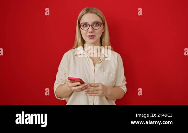 Joyful young blonde woman, alone over red background, confidently ...